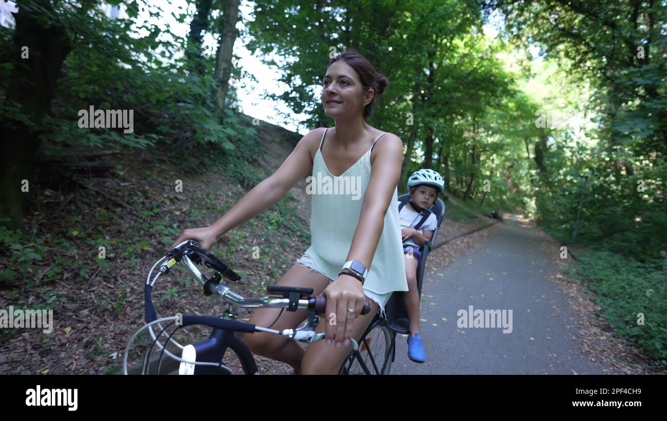 Parent riding bicycle with child in bike seat in fore pathway. Mother ...