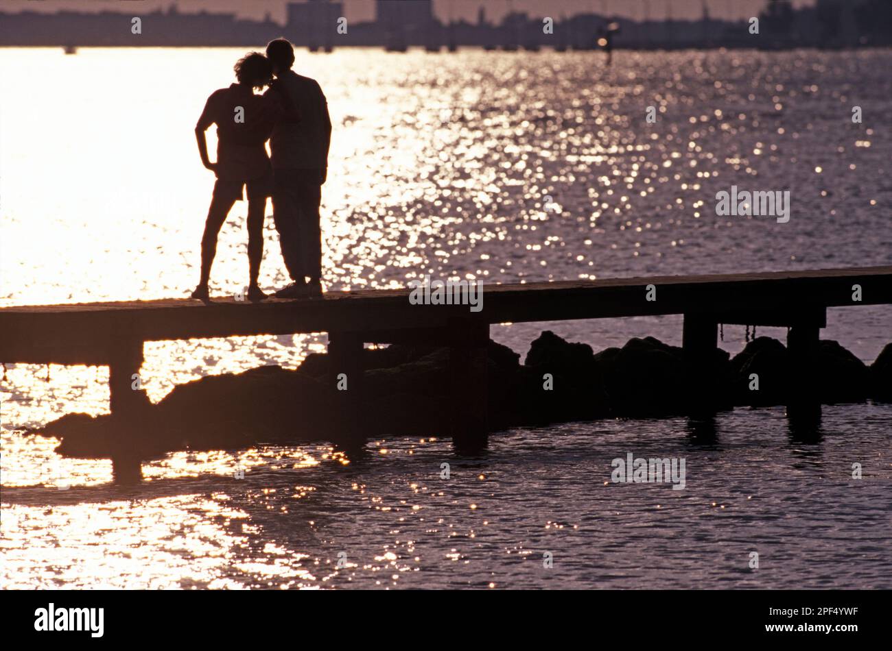 Romantic couple snuggling on a pier at sunset Stock Photo - Alamy