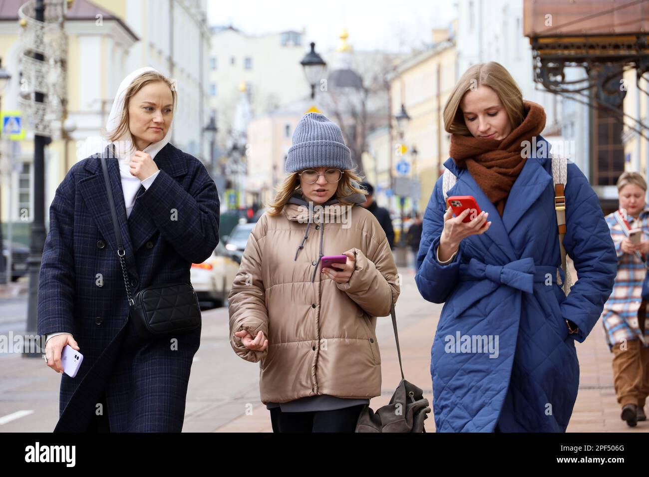 People using smartphones on city street. Young women in spring clothes ...