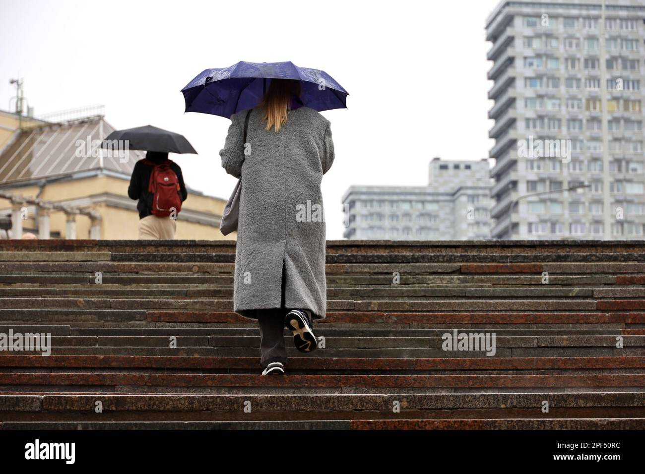 Woman with umbrella walking up the steps on city buildings background ...