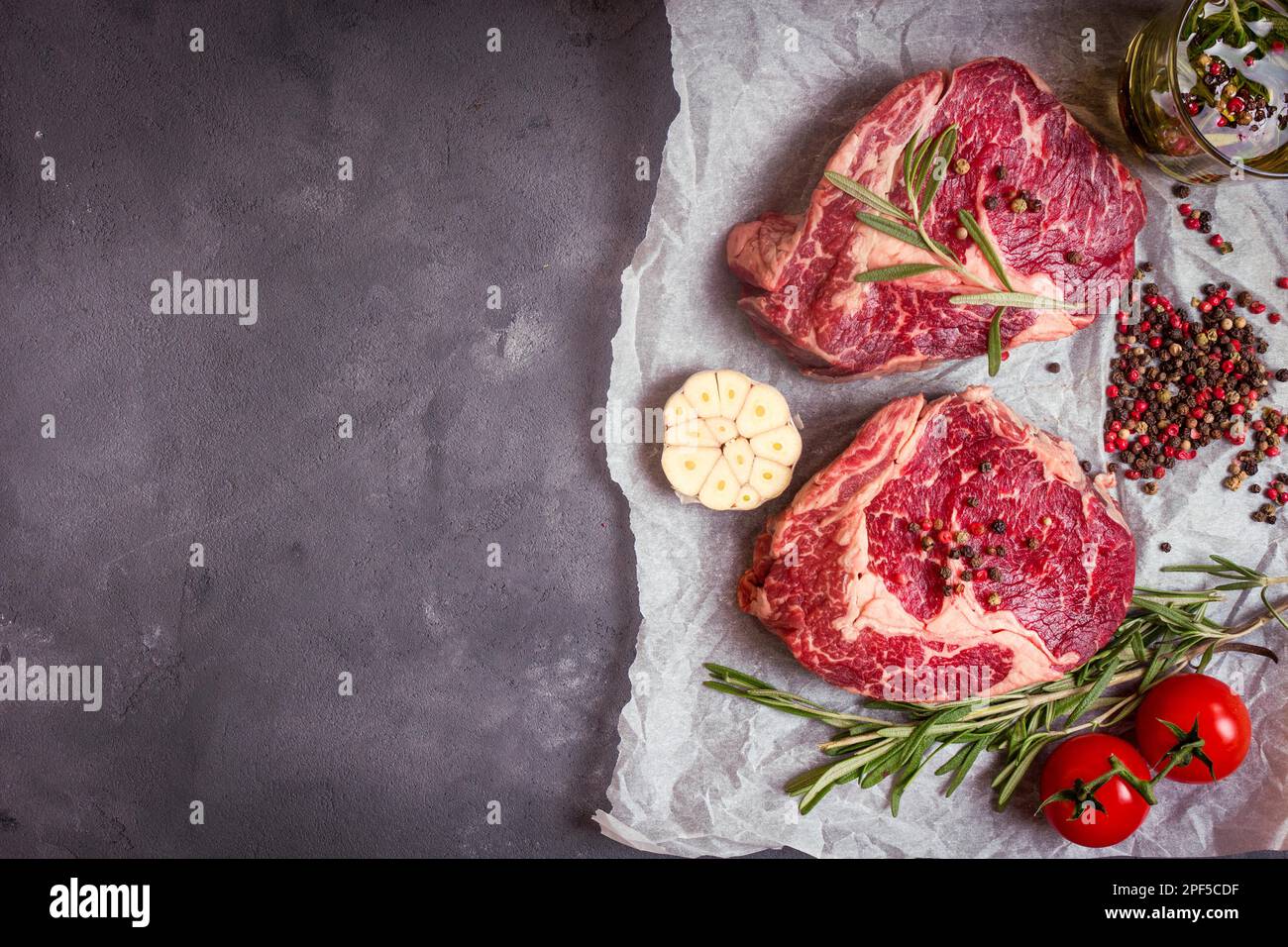 Raw Juicy Ribeye Steaks With Seasonings Ready For Roasting On Baking Paper Rustic Concrete