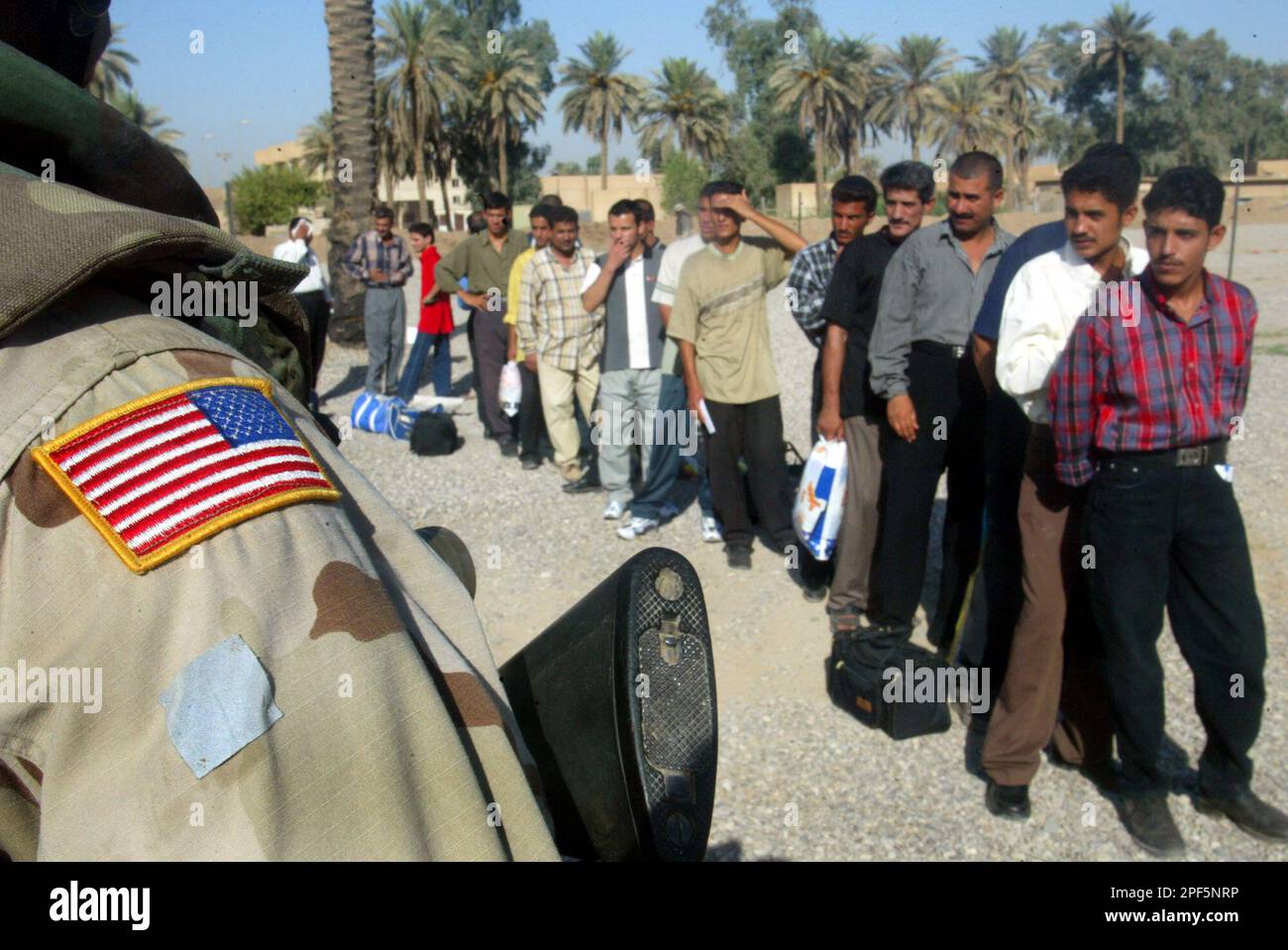 A U.S. soldier stands guard as newly recruited Iraqi soldiers, wait in ...