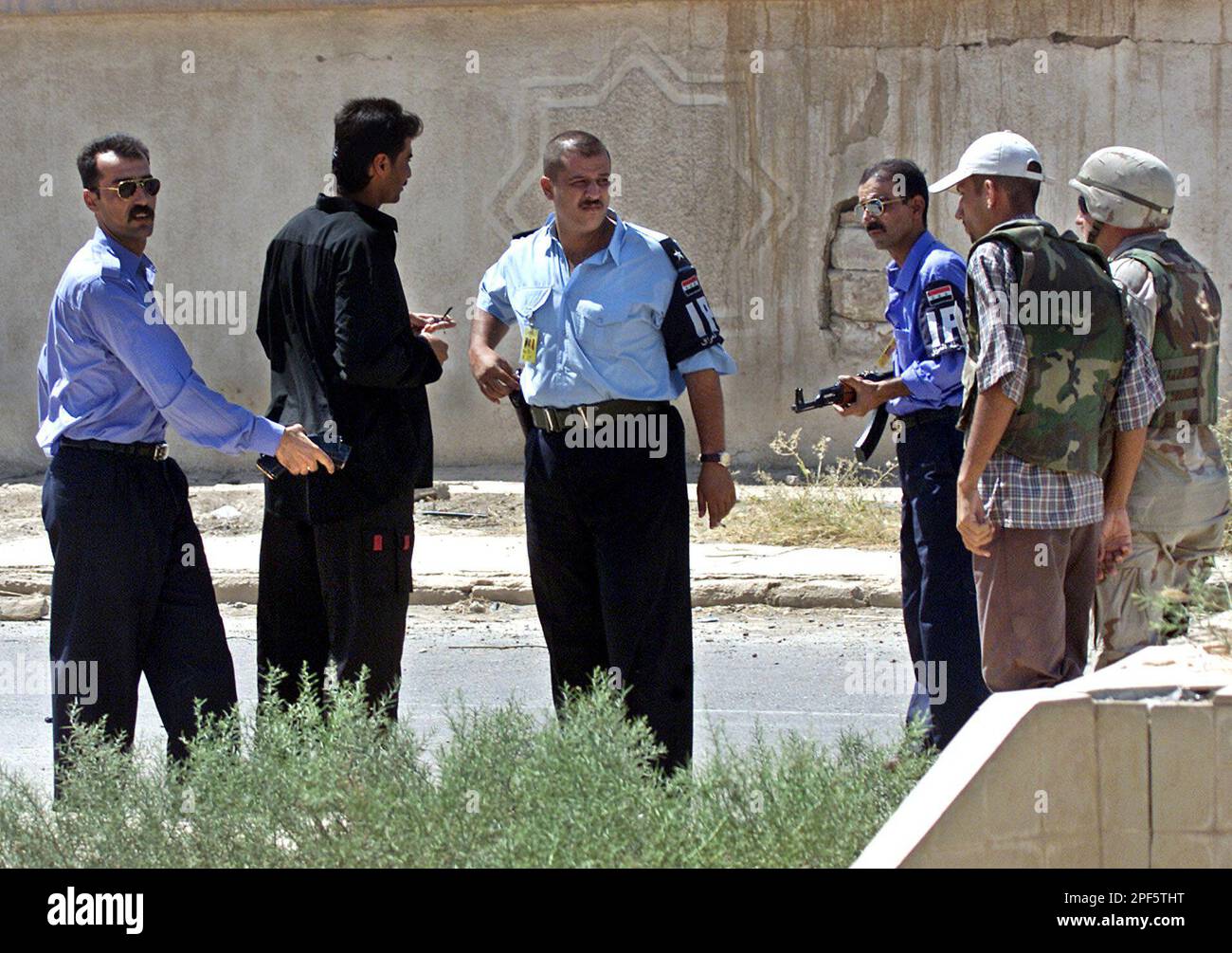 Iraqi police officers frisk a man, second left, as U.S. military police ...