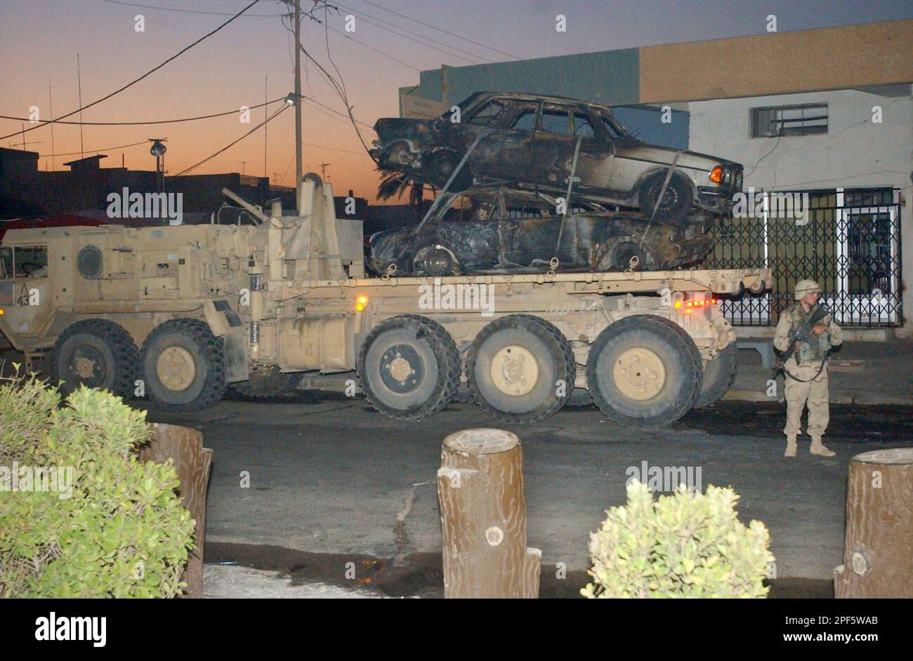 U.S. troops guard a flatbed truck carrying two vehicles that were ...
