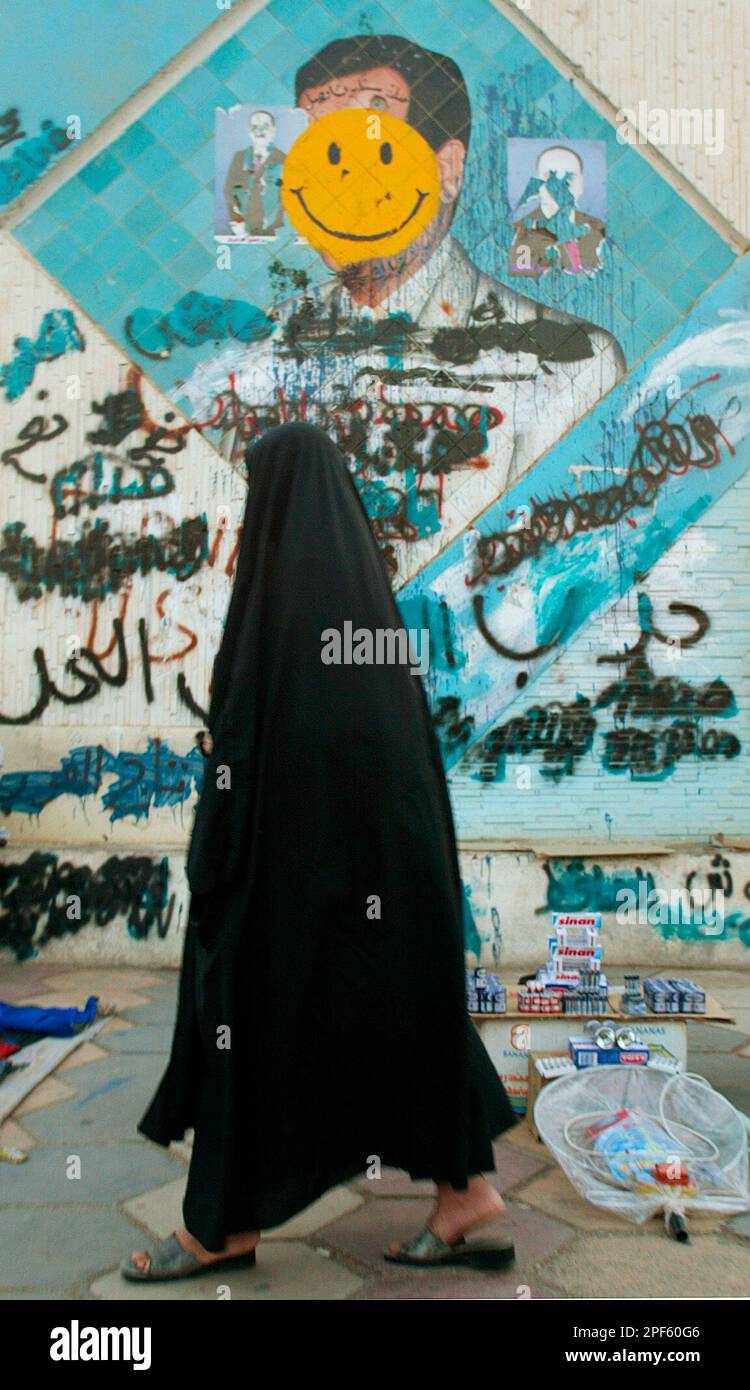 An Iraqi woman walks past a portrait of Saddam Hussein that has been ...