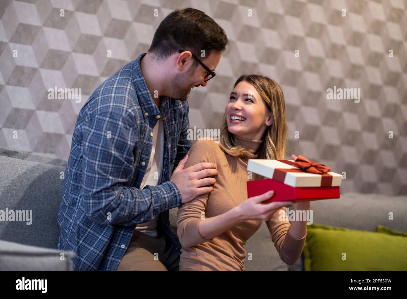 Young woman receiving a surprise gift box from her boyfriend at home ...