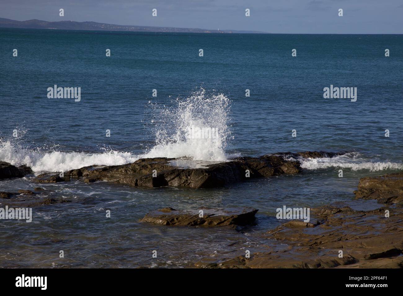 A powerful wave crashes against a rocky shoreline, creating an ...