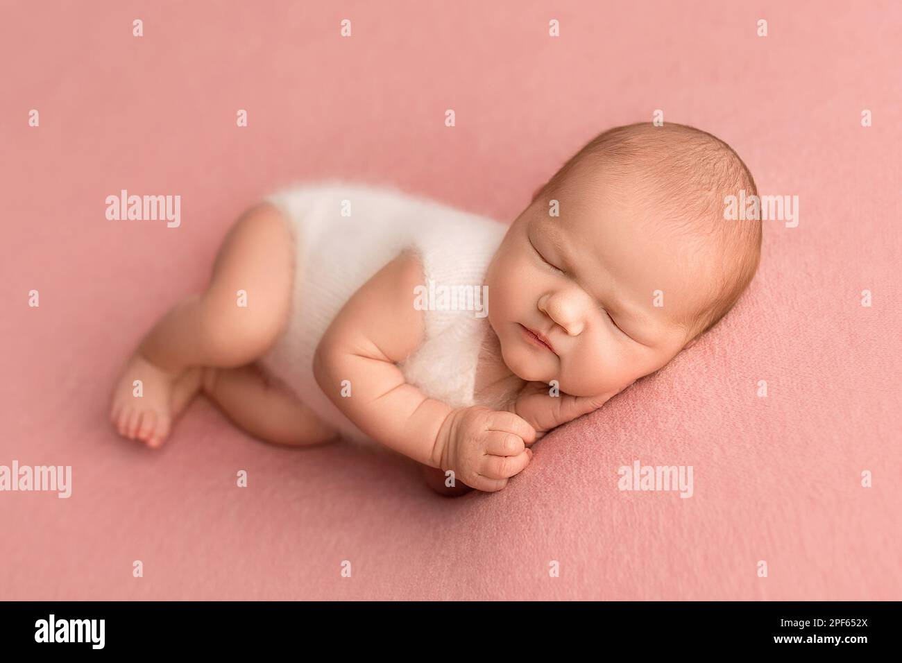 Top view of a newborn baby girl sleeping in a white overalls on a pink ...