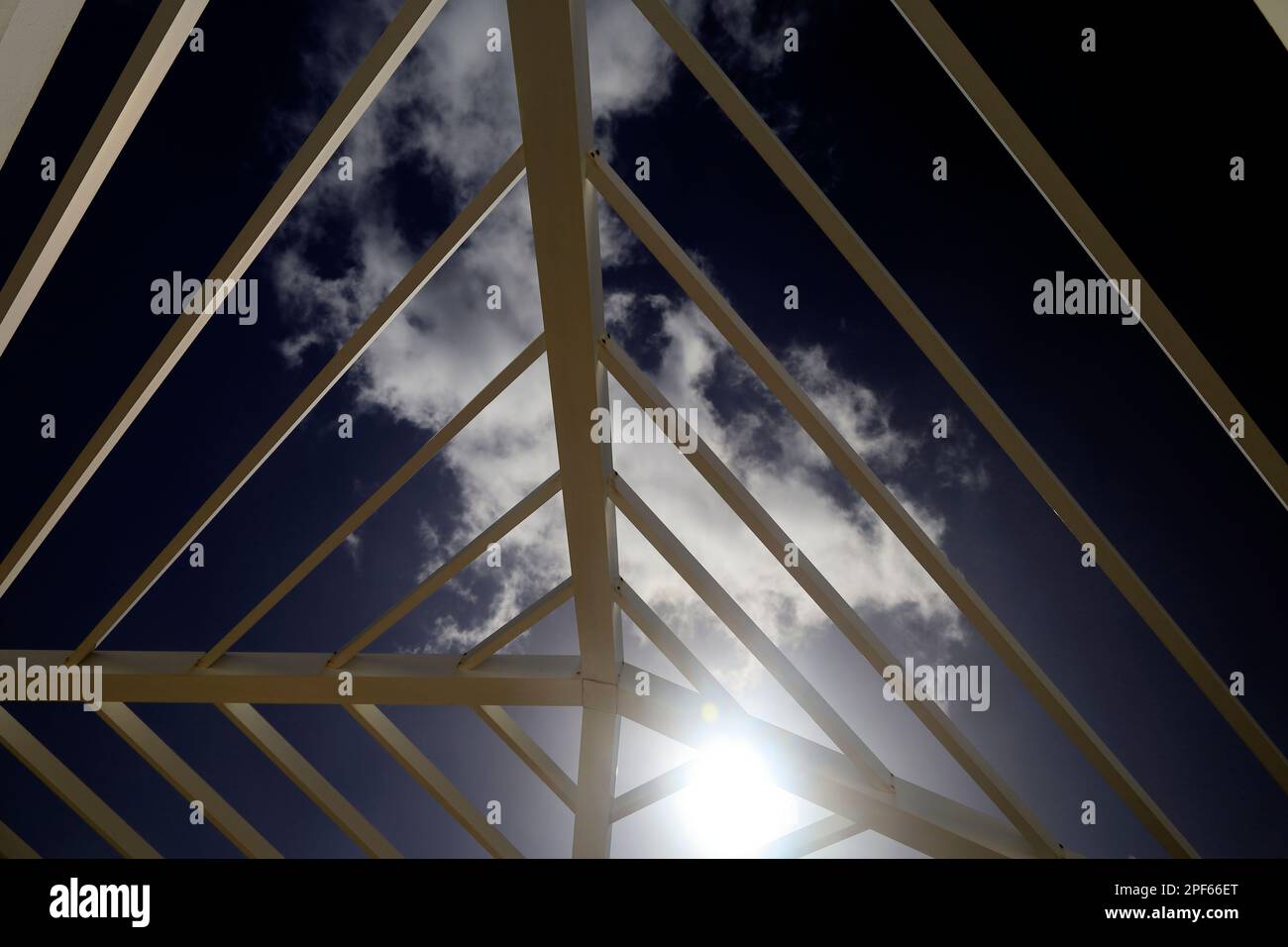 Blue sky, sun and clouds through framework of a pergola. Abstract ...