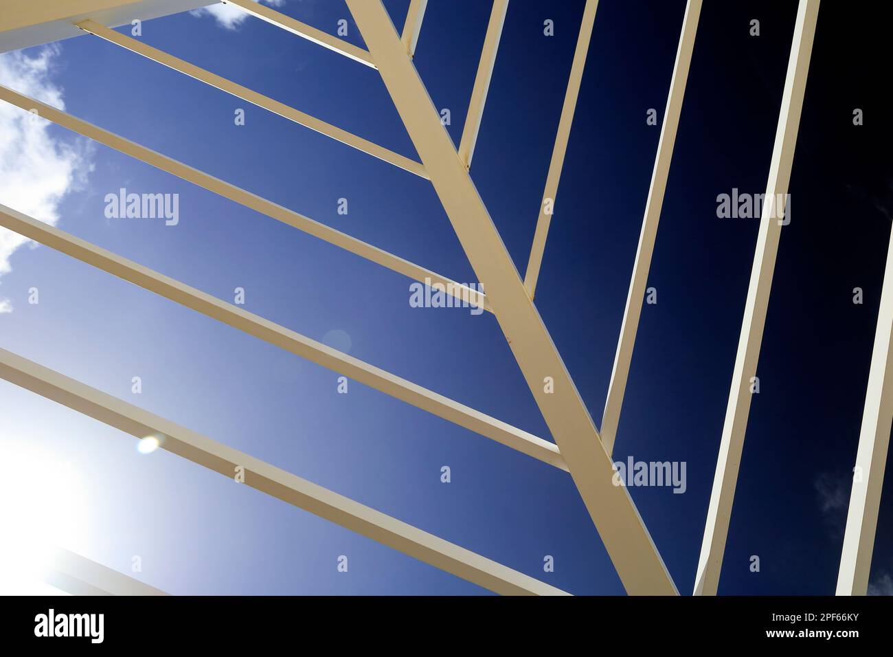 Blue sky, sun and clouds through framework of a pergola. Abstract ...
