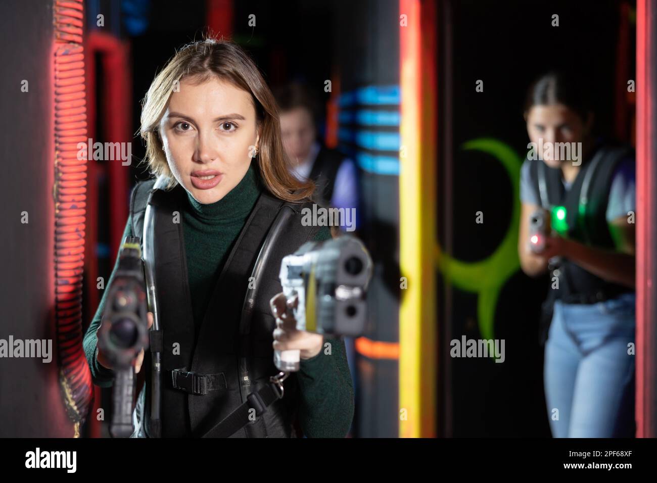 Joyous girl with laser pistol playing laser tag with friends on ...