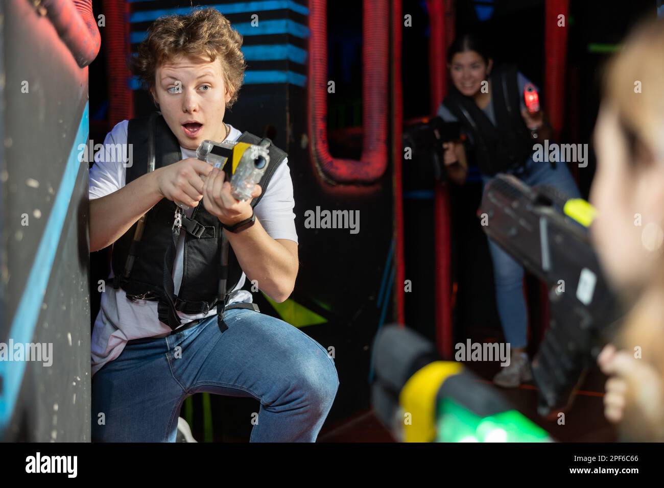 Emotional man with laser pistol playing laser tag with friends on dark ...