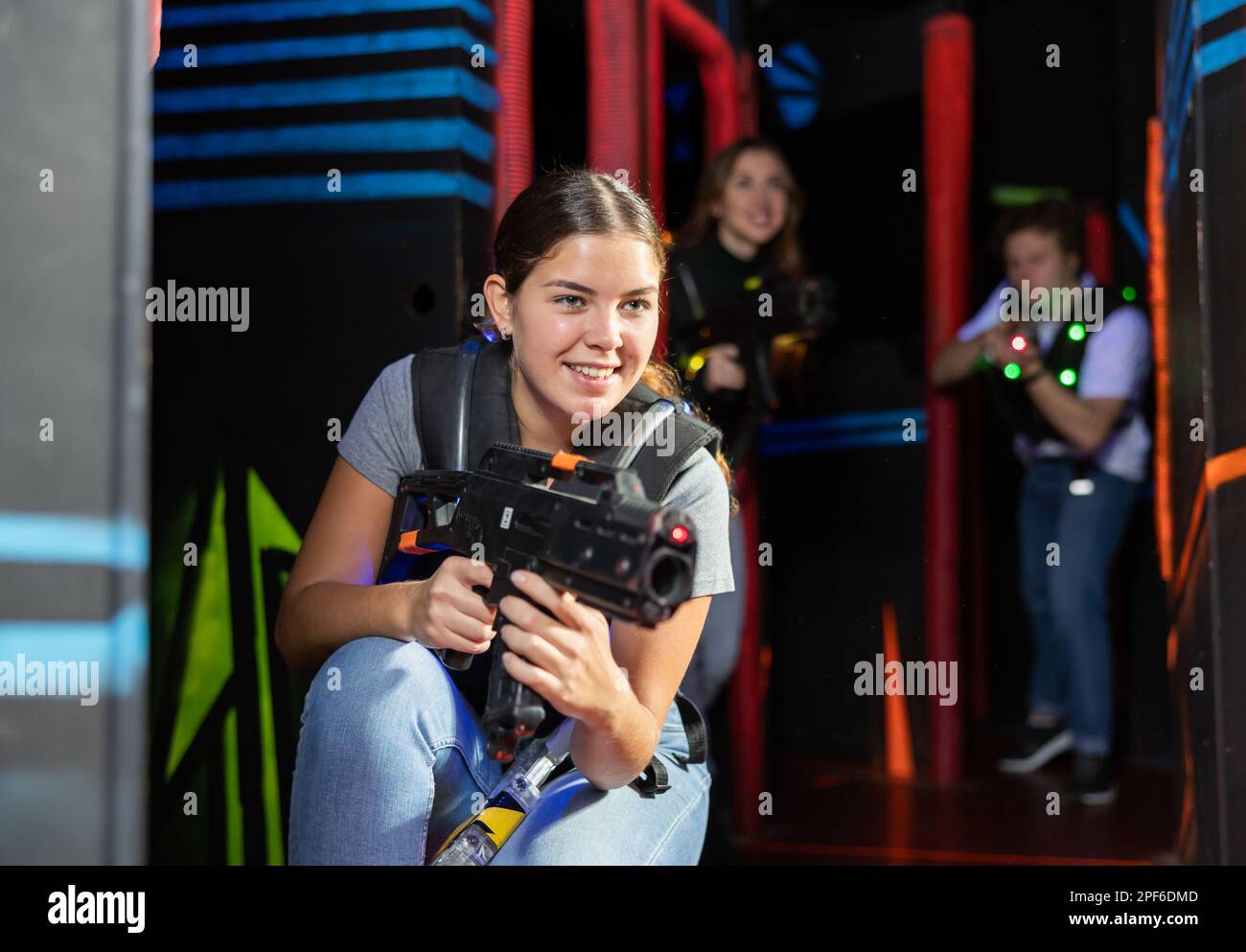 Positive girl holding laser pistol playing laser tag game with friends ...