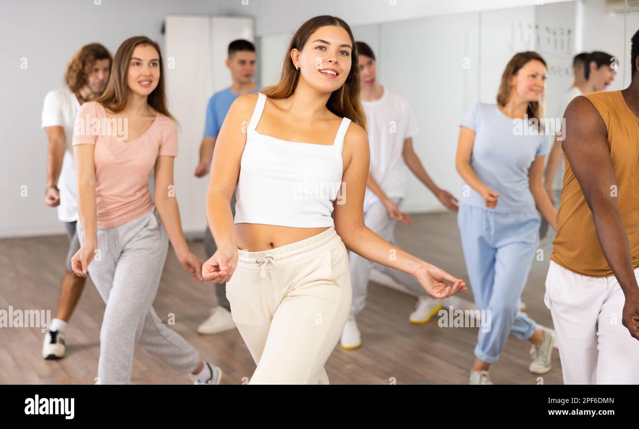 Class of active young adult dancers performing steps during exercising ...