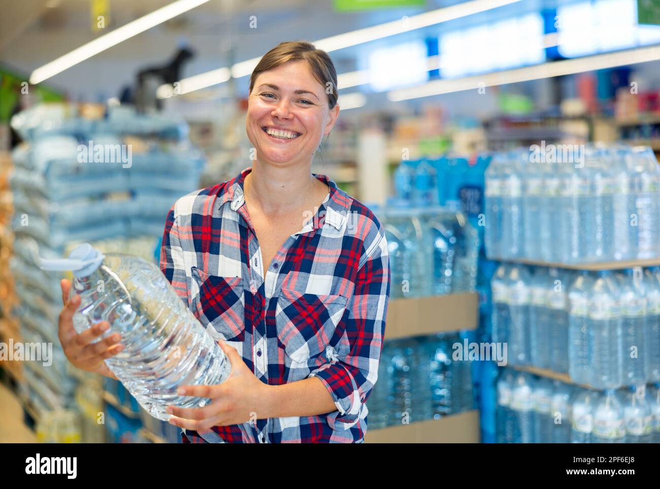 Portrait of attractive woman choosing water in bottle at supermarket ...