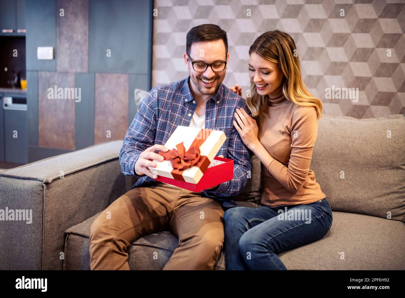 Young woman receiving a surprise gift box from her boyfriend at home ...