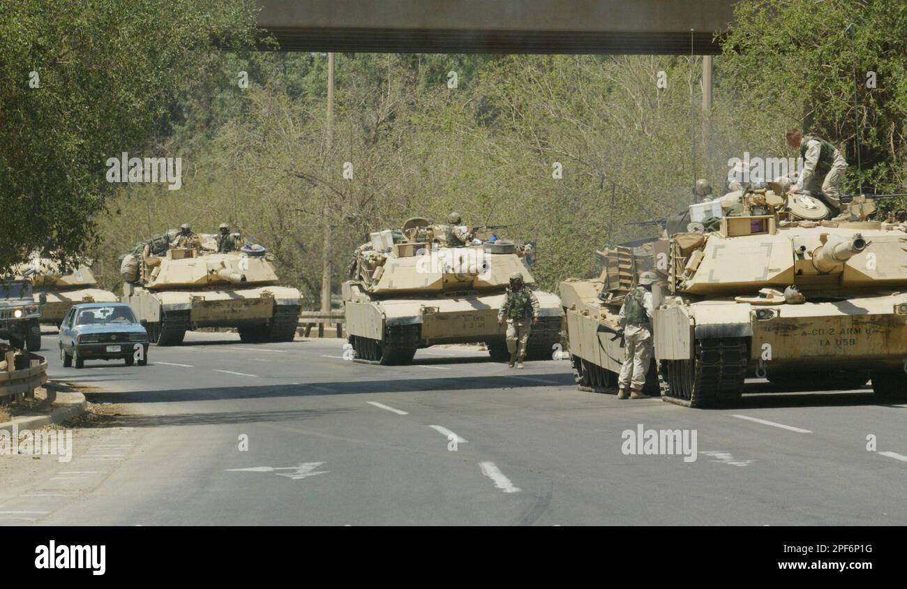 A column of US Army Abram tanks pause along a highway towards the city ...