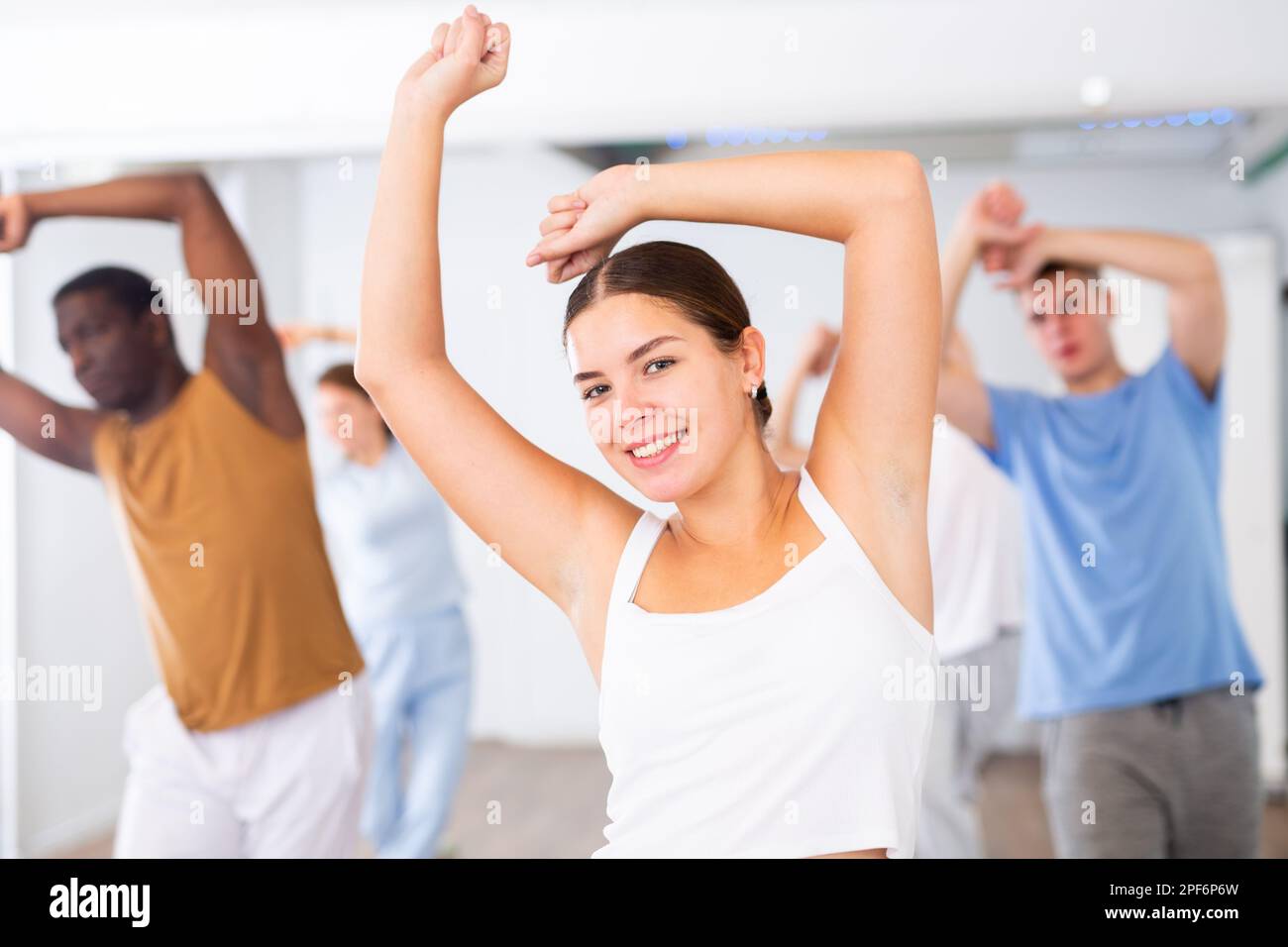 Group of young adult dancers raising both hands up during exercising in ...