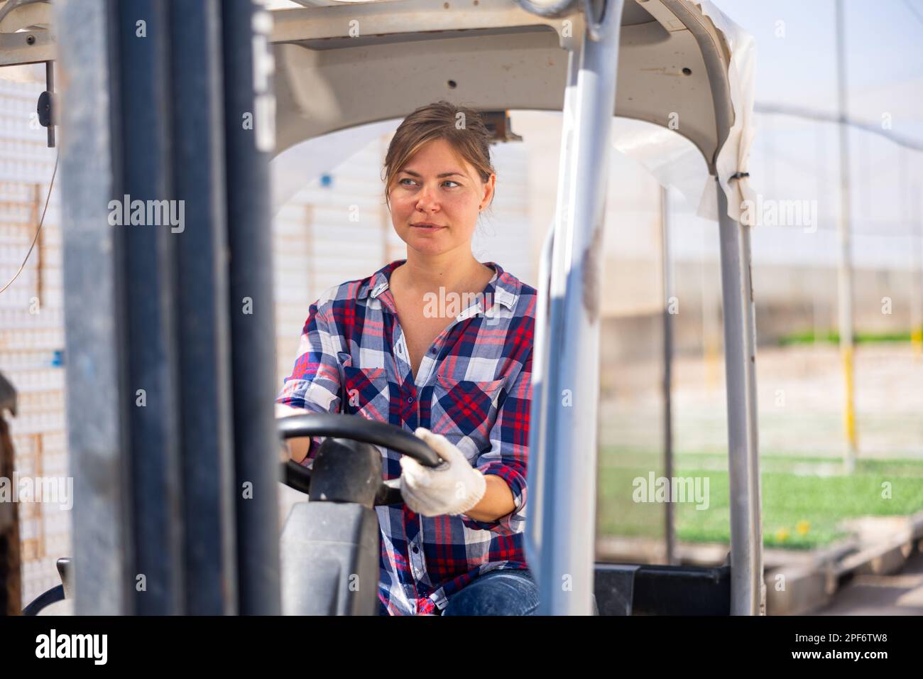 Experienced farmer woman working on forklift loader at farm greenhouse ...