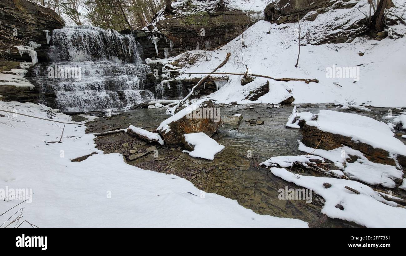 A winter scene featuring a waterfall cascading down a rocky cliff amid ...