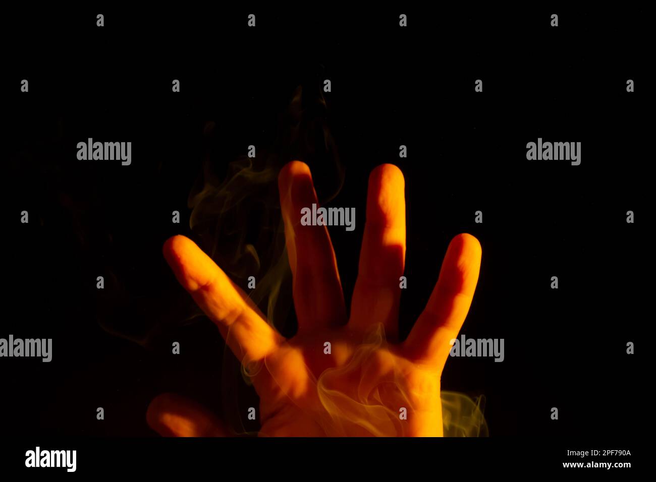A male hand lit yellow with smoke around it isolated on a black ...