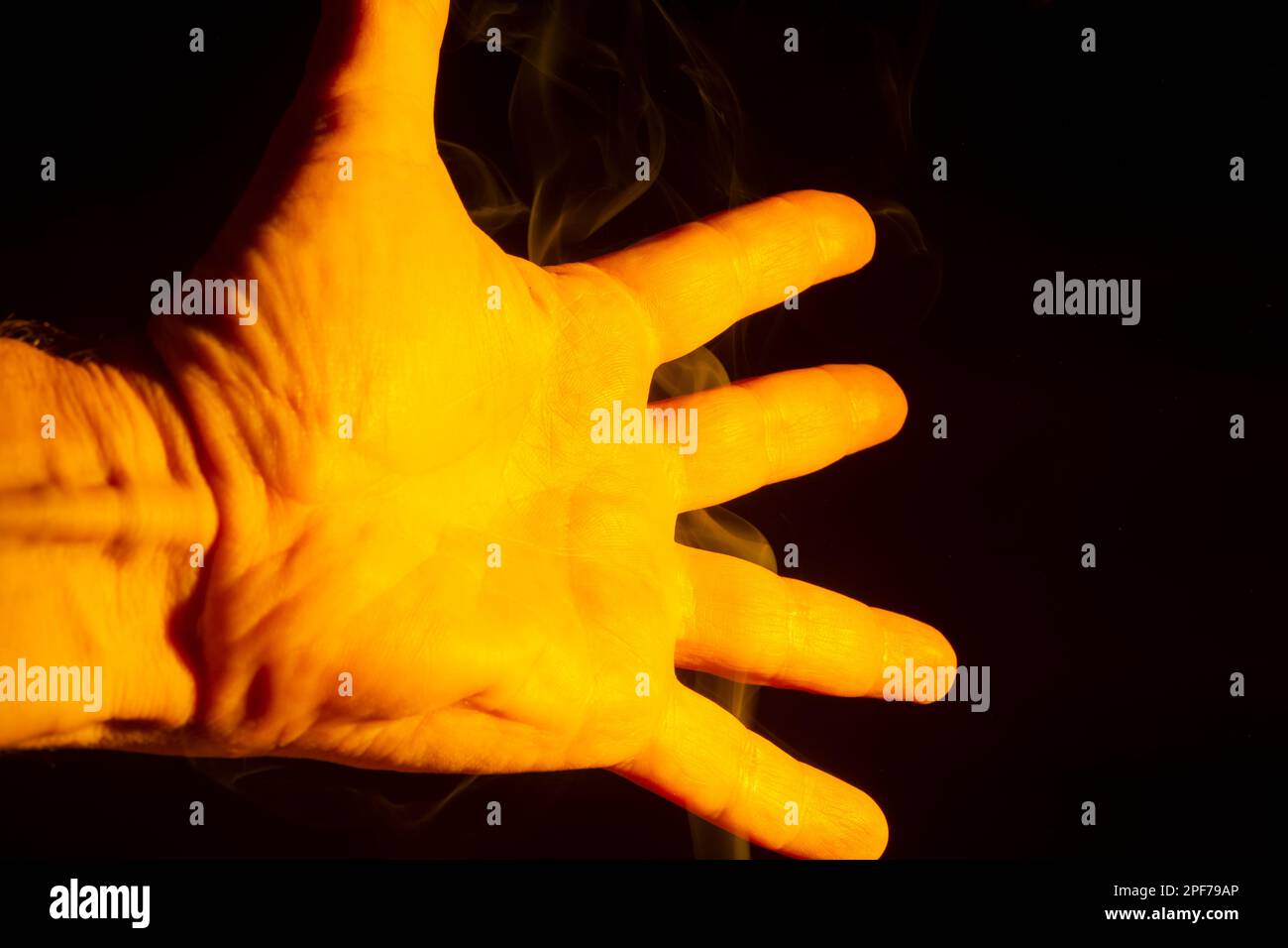 A male hand lit yellow with smoke around it isolated on a black ...