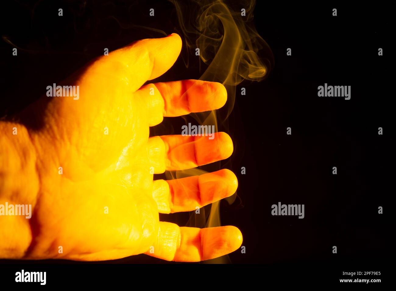 A male hand lit yellow with smoke around it isolated on a black ...