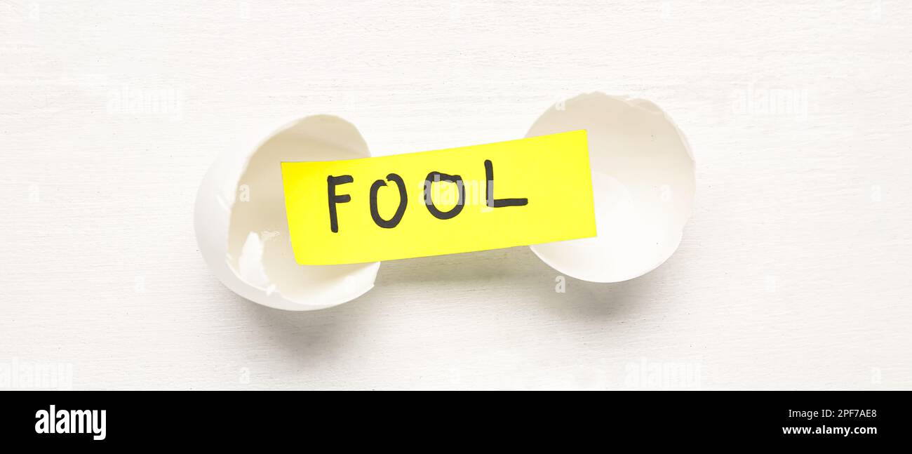 Paper with word FOOL and egg shell on white wooden background Stock ...