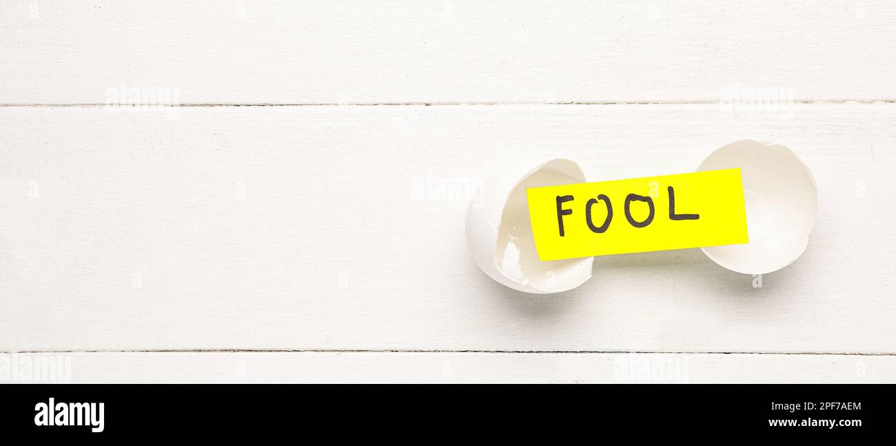 Paper with word FOOL and egg shell on white wooden background with ...