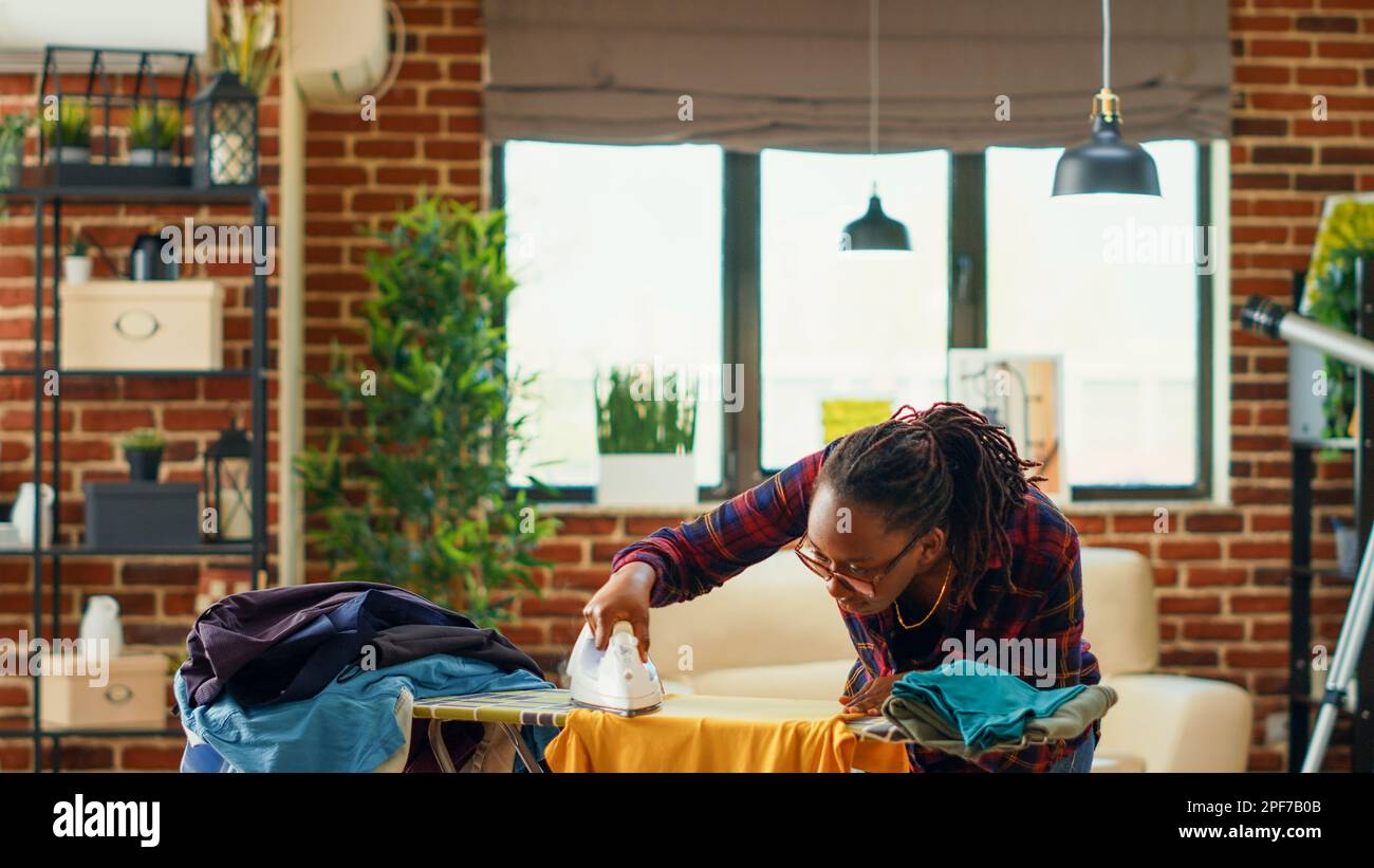 African american woman using steam iron and ironing board, smoothing ...