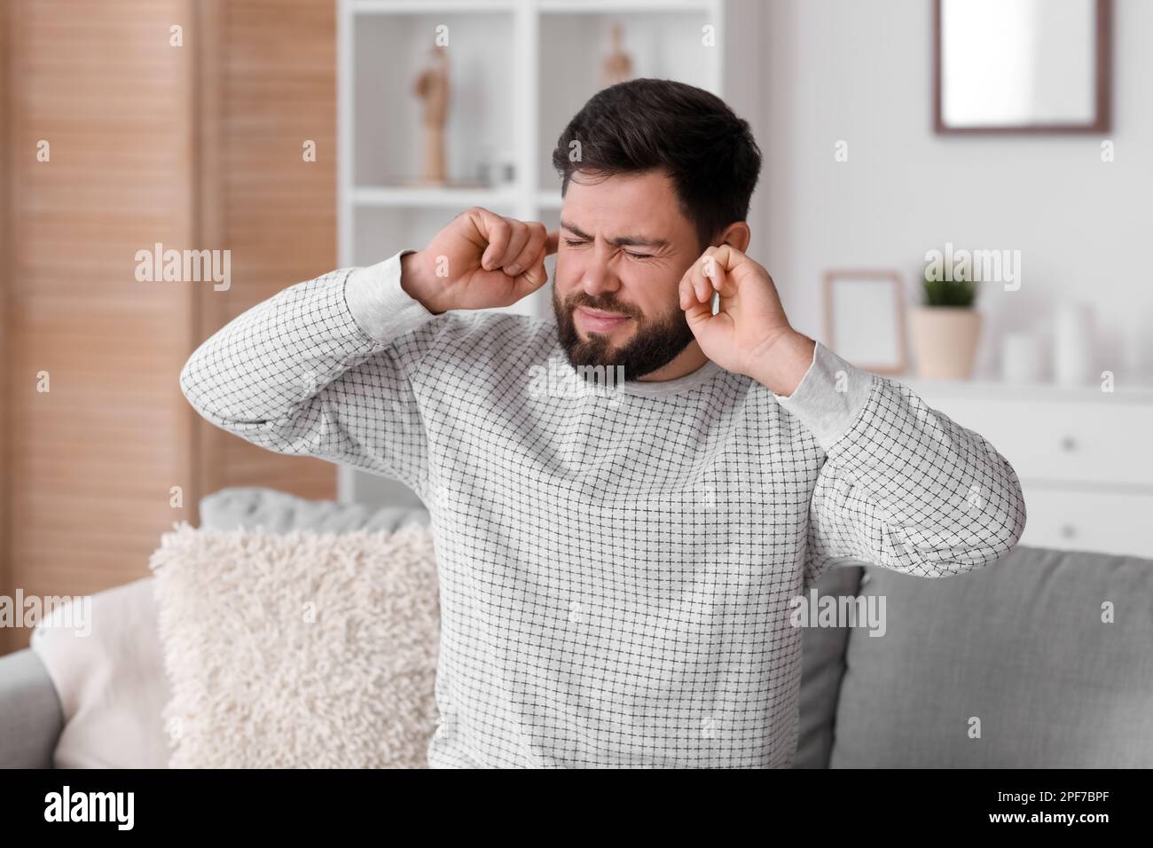 Angry young man suffering from loud noise at home Stock Photo - Alamy