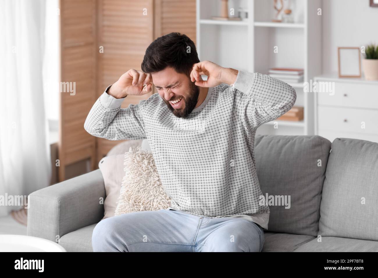 Angry young man suffering from loud noise at home Stock Photo - Alamy