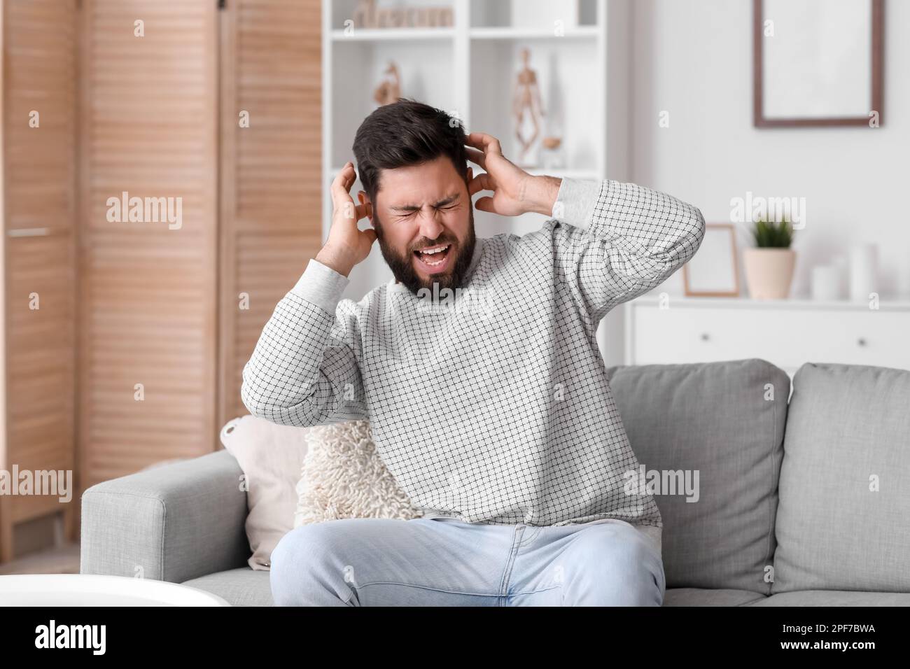 Angry young man suffering from loud noise at home Stock Photo - Alamy
