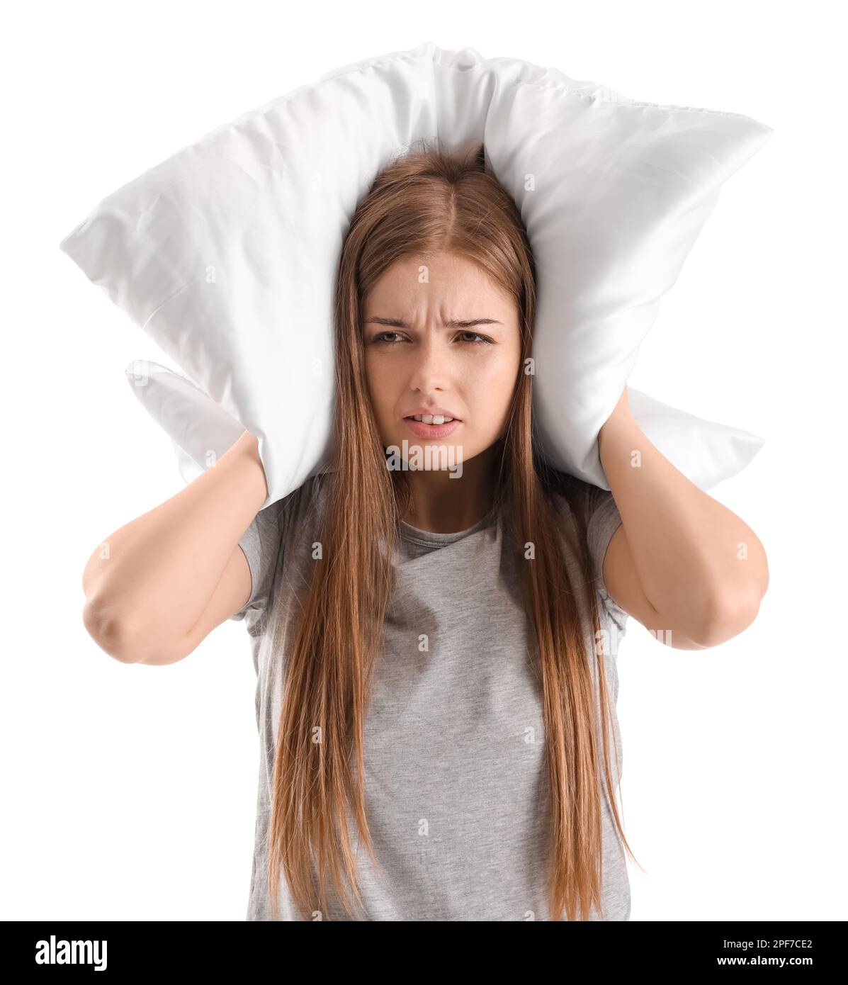 Irritated young woman with pillow suffering from loud noise on white ...