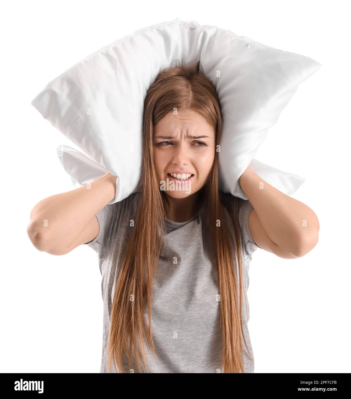 Irritated young woman with pillow suffering from loud noise on white ...