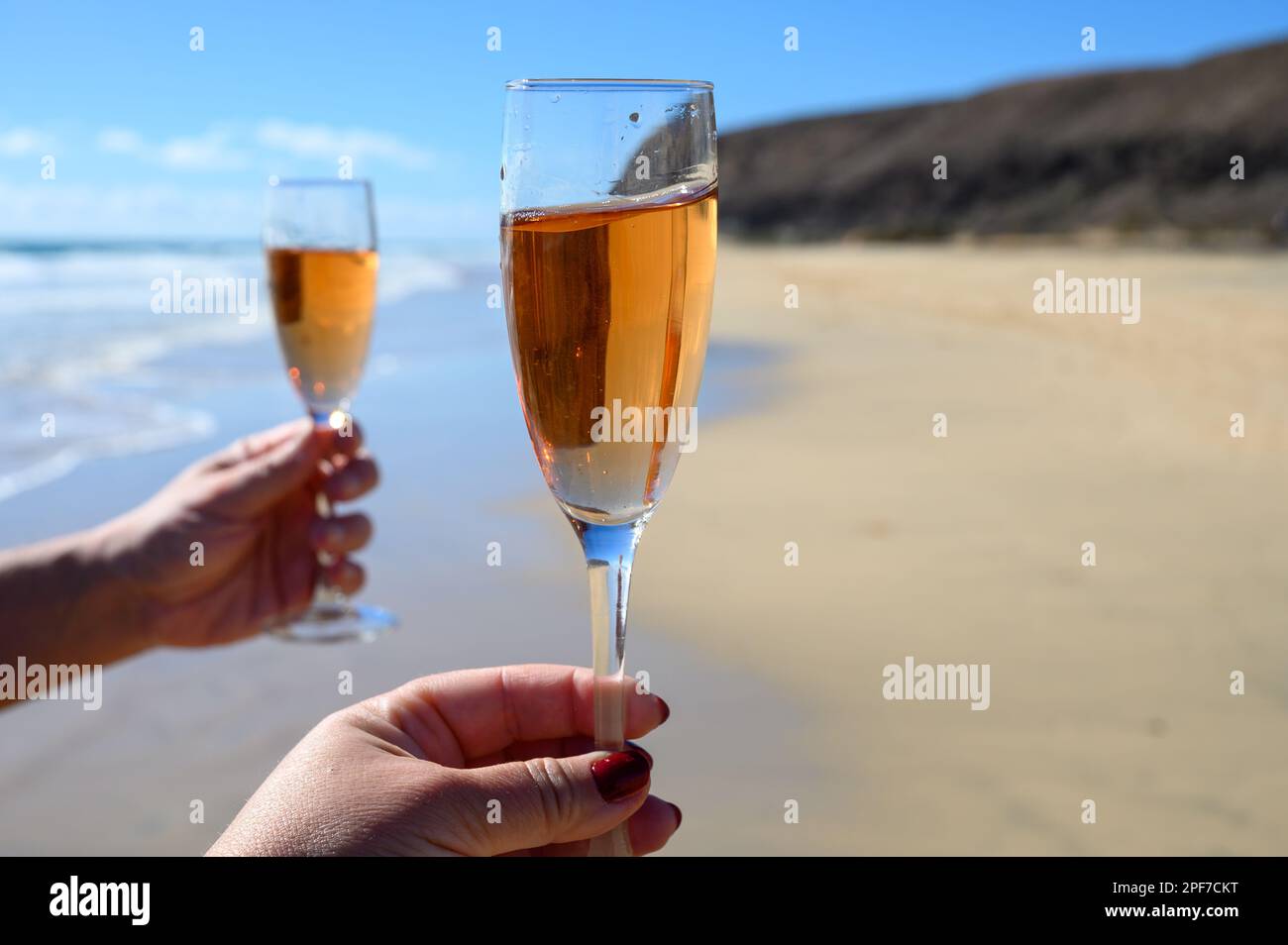 Beach party, hands with glass of rose champagne or cava sparkling wine ...