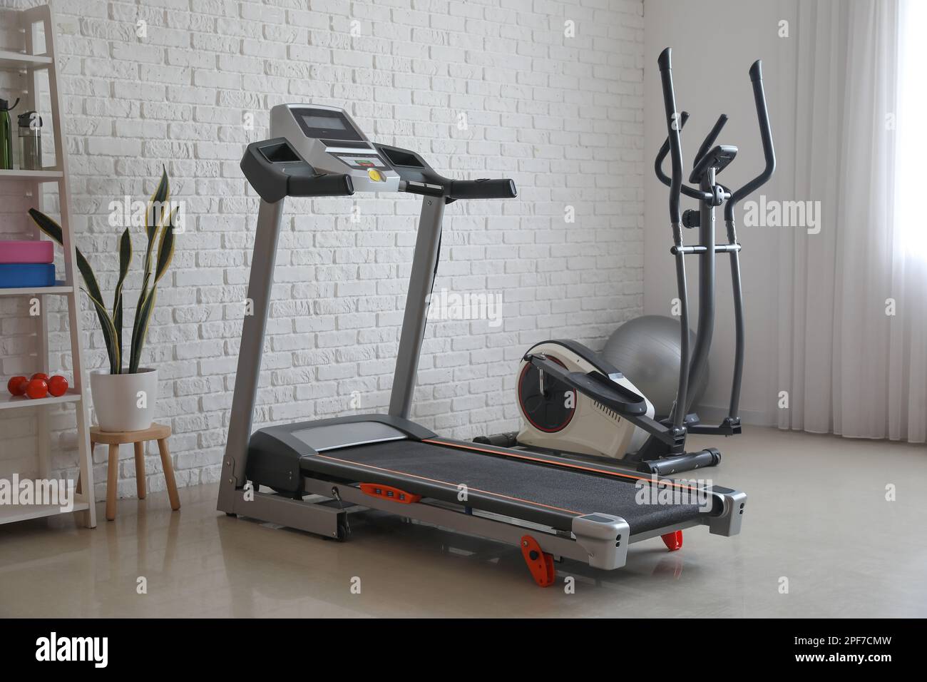 Interior of gym with modern treadmill and elliptical trainer near white ...
