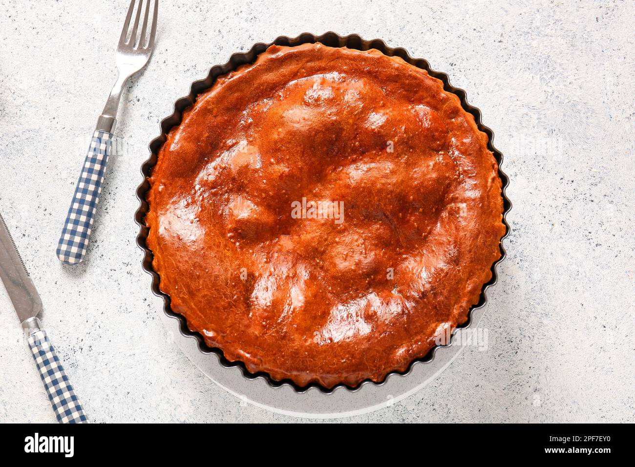 Delicious meat pie in baking form and cutlery on white grunge table ...