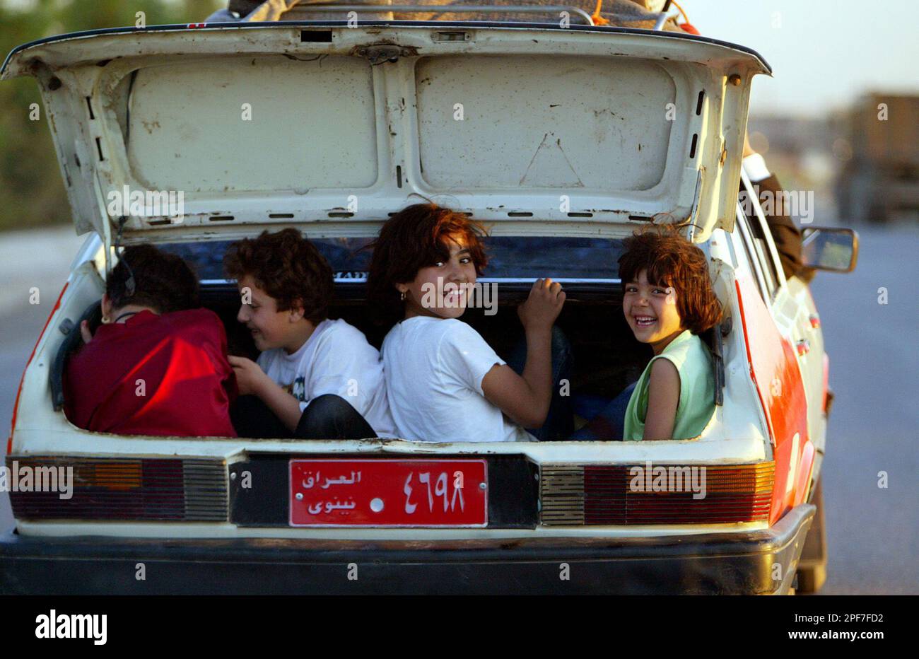 Iraqi Kurdish girls smile as they ride in the trunk of a speeding taxi ...