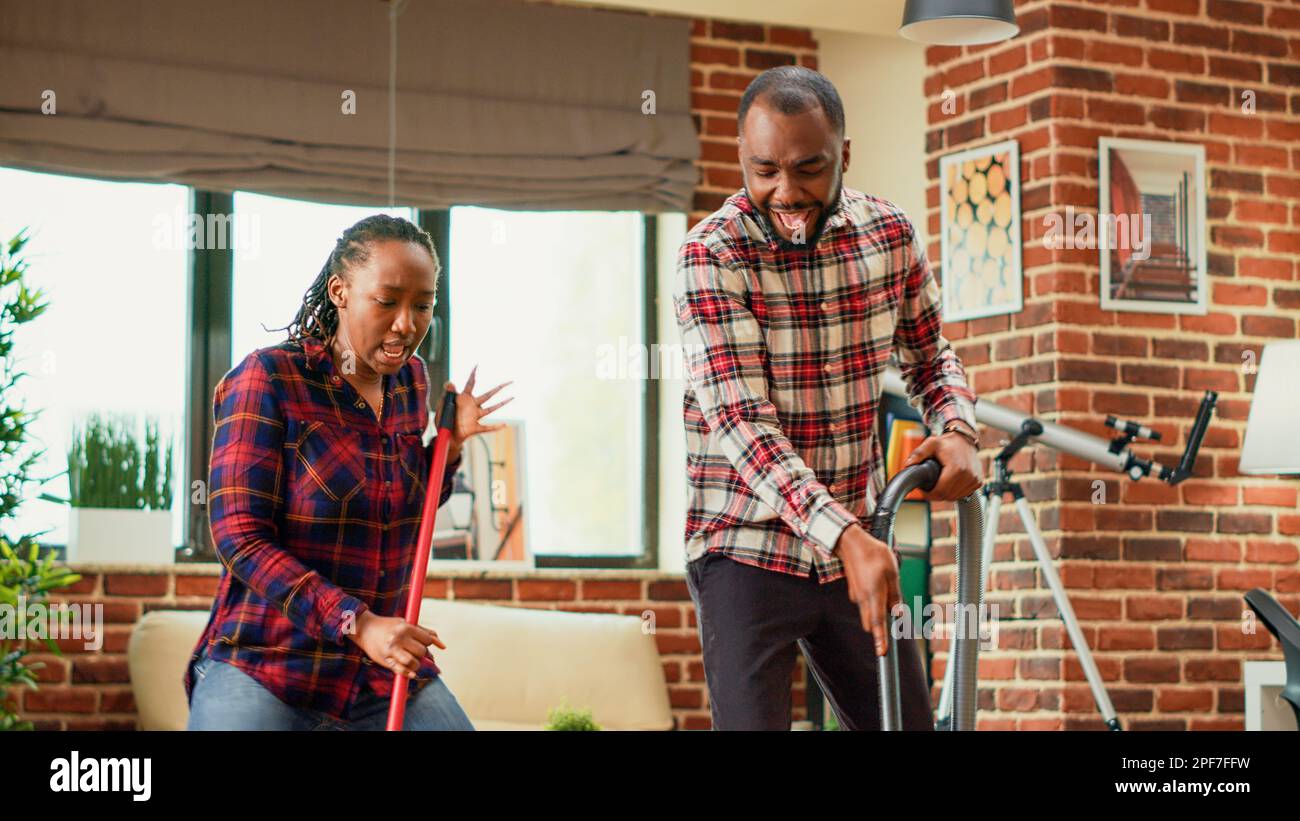 Modern young couple singing and doing chores together, having fun with ...