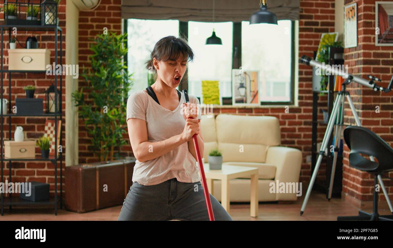 Smiling person cleaning living room floors with mop, listening to music ...