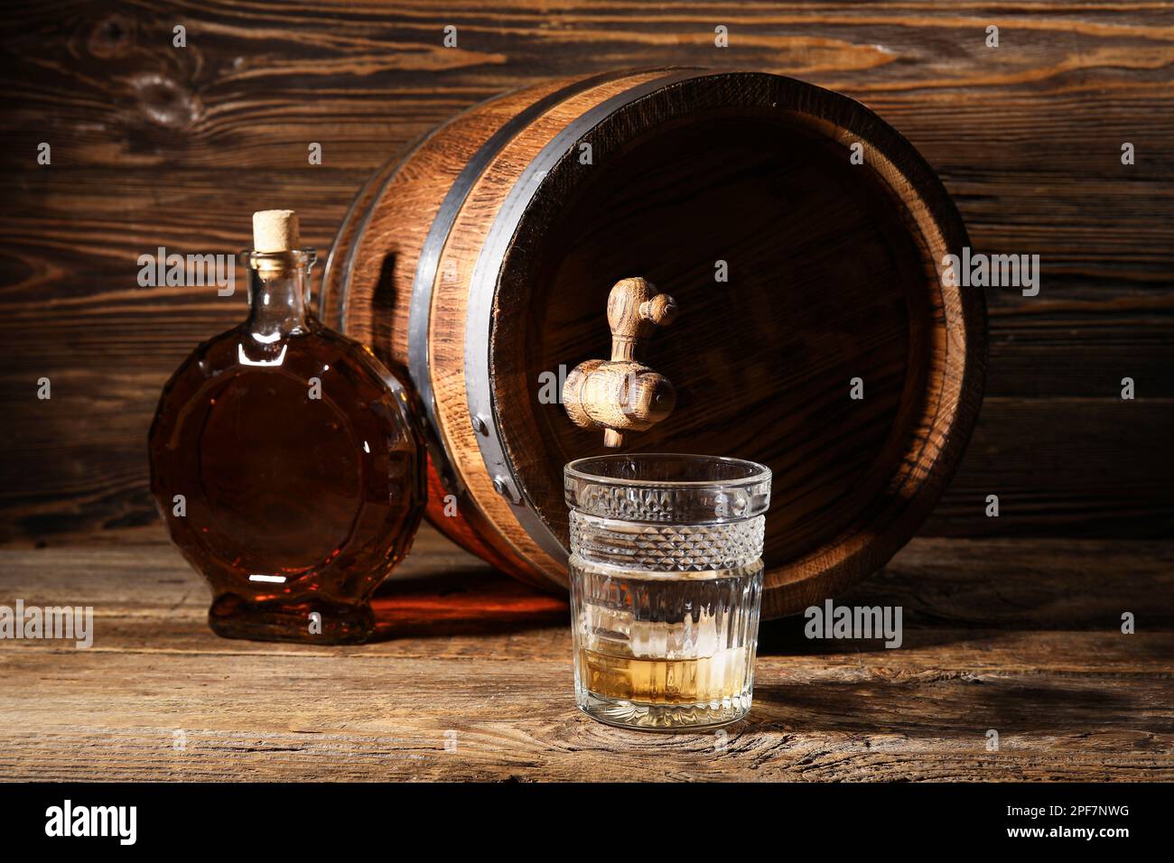 Bottle and glass of cold whiskey with oak barrel on wooden background ...
