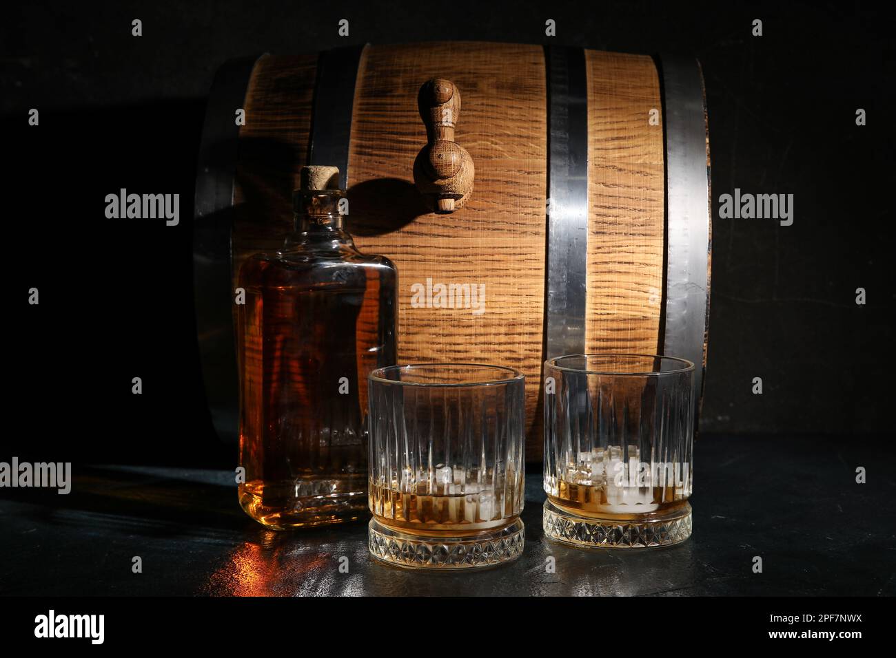 Glasses and bottle of cold whiskey with oak barrel on dark background ...