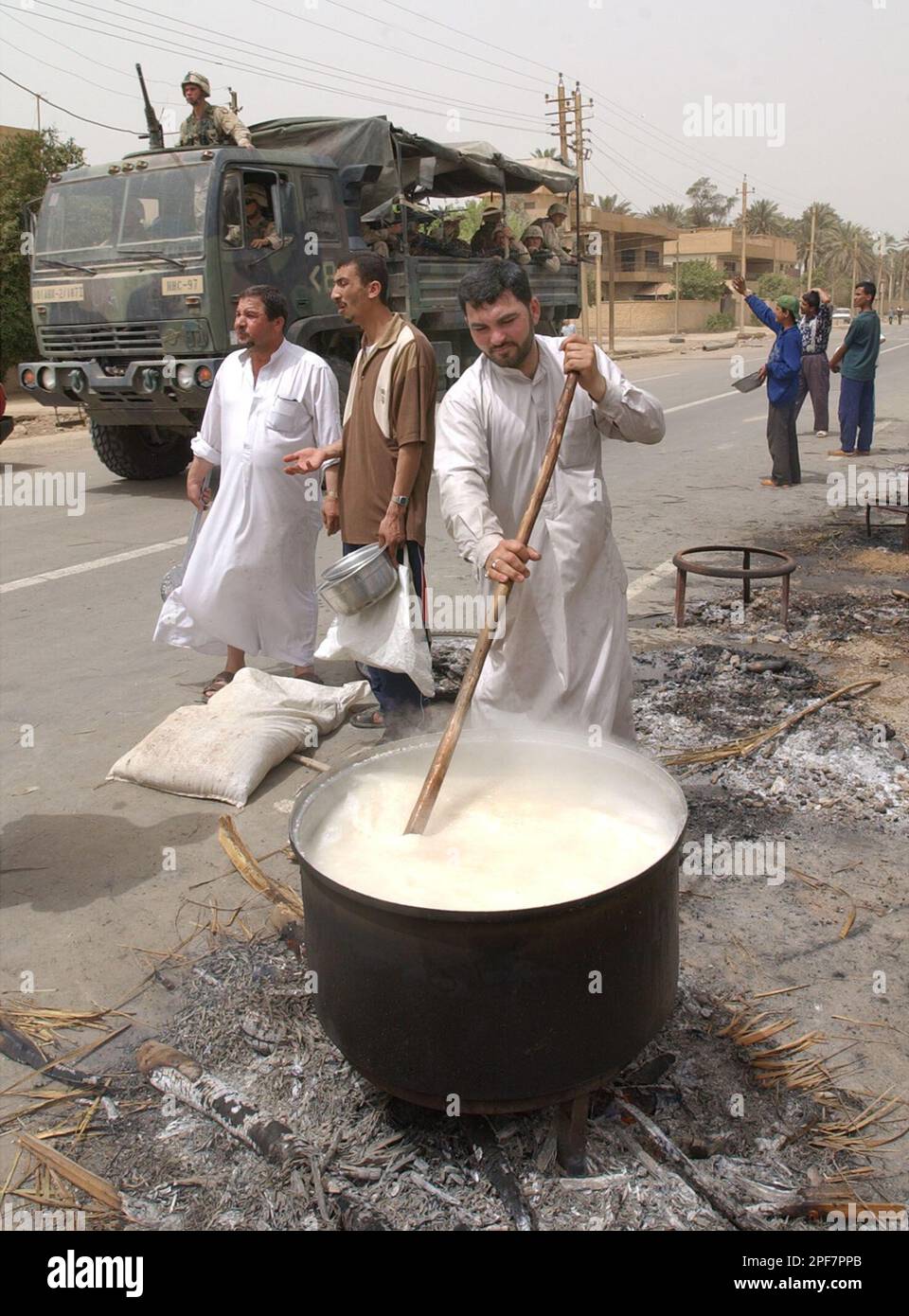 An Iraqi Shiite man boils rice in the street as a U.S army truck passes ...