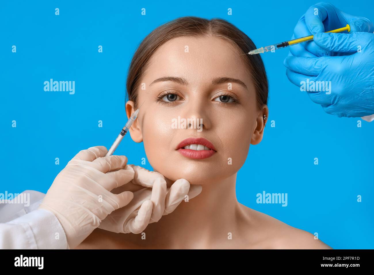Young woman receiving filler injections in face against blue background ...