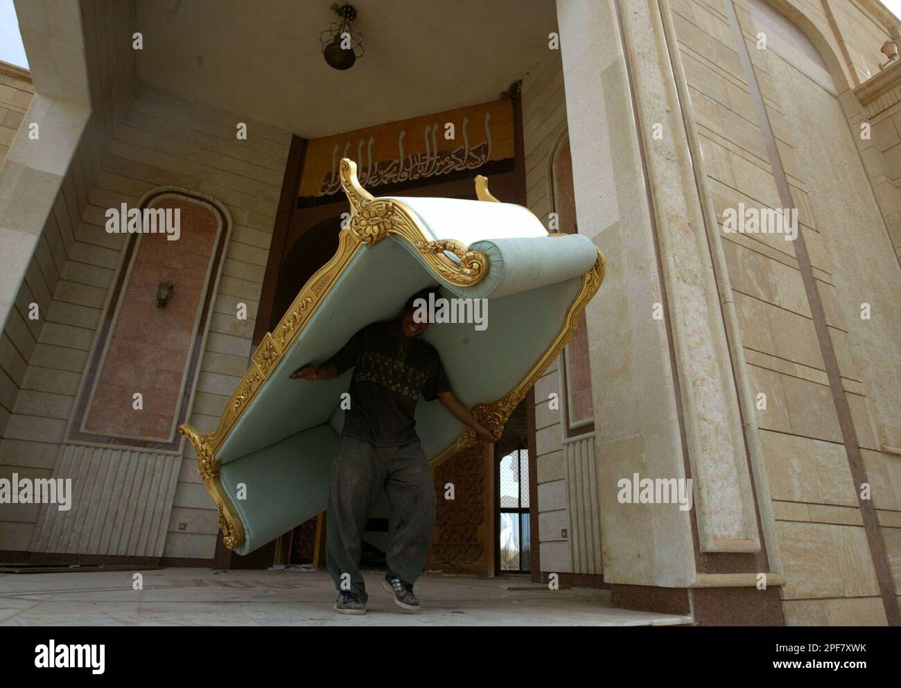 An Iraqi man trudges under the weight of a couch he looted from a gated ...