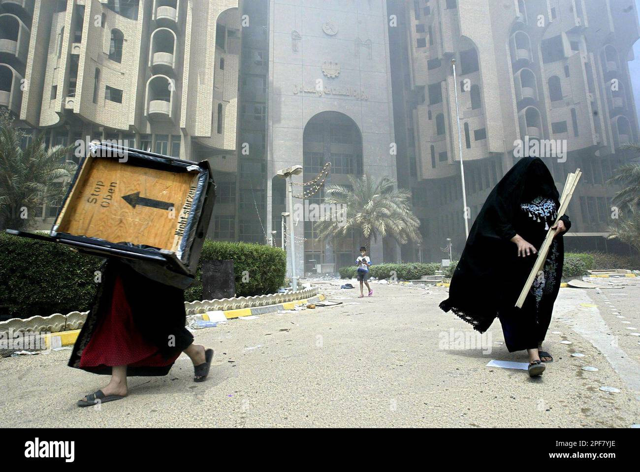 Two Iraqi women carry furniture away from an Iraqi government office ...