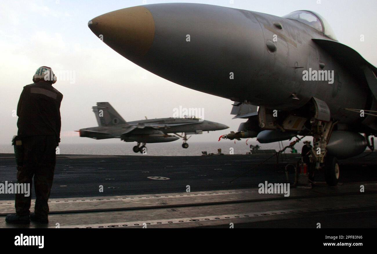 An aircraft officer stands near a F/A-18 Hornet, watching another ...