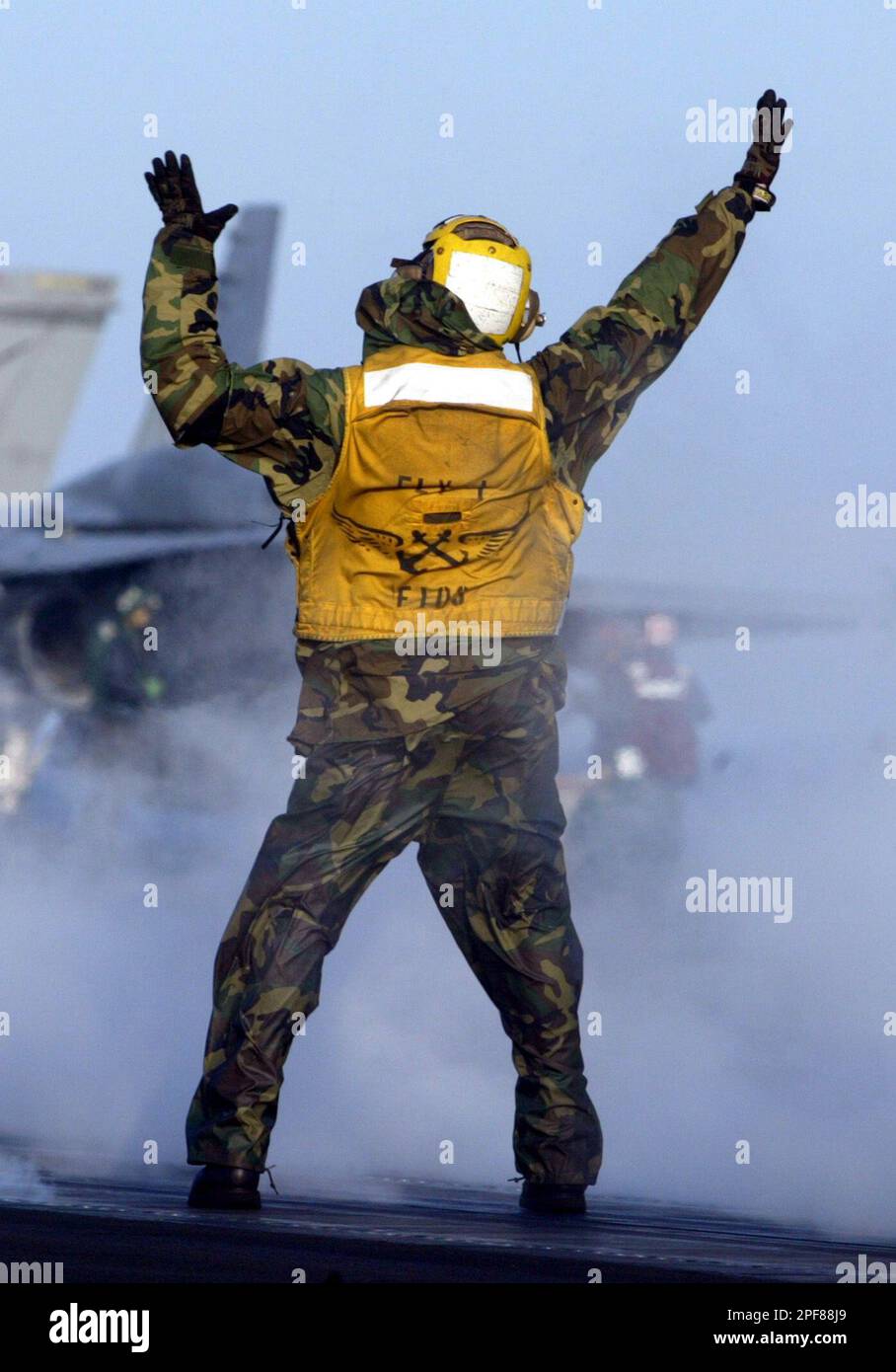 An aircraft handling officer makes hand signals to an aircraft on the ...
