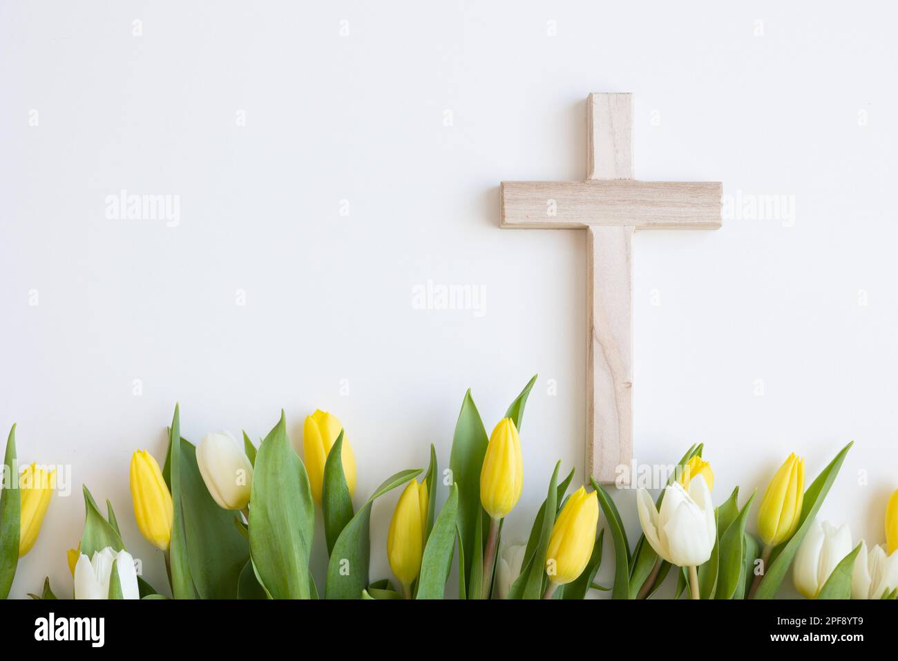 Simple wood Christian cross with yellow and white tulips on a white ...